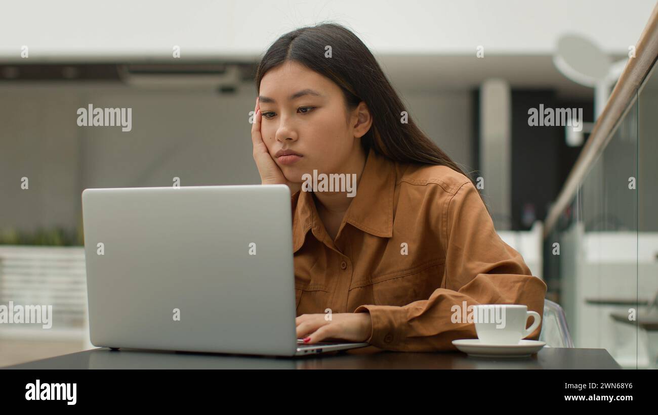 Tired bored Asian businesswoman girl sit in cafe working on laptop sad ...