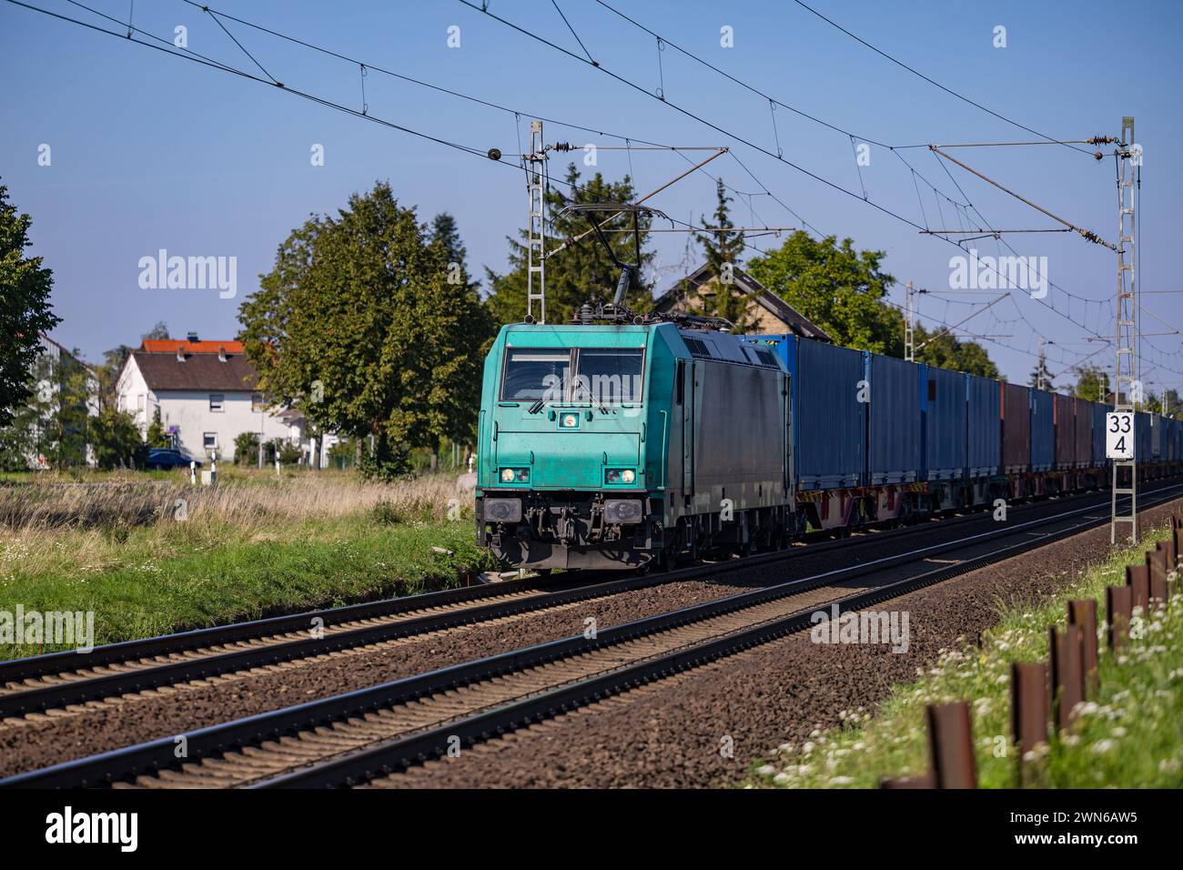 A turquoise freight train on an electric railroad line through a rural ...