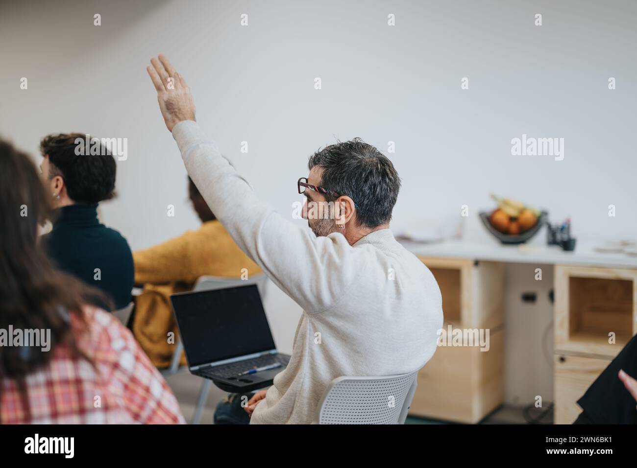 Adult student raising hand in a classroom environment seeking attention ...