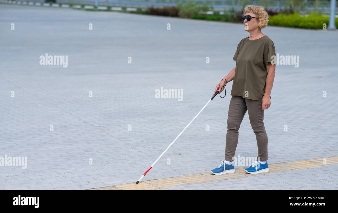 An elderly blind woman walks with a cane along a tactile tile Stock ...
