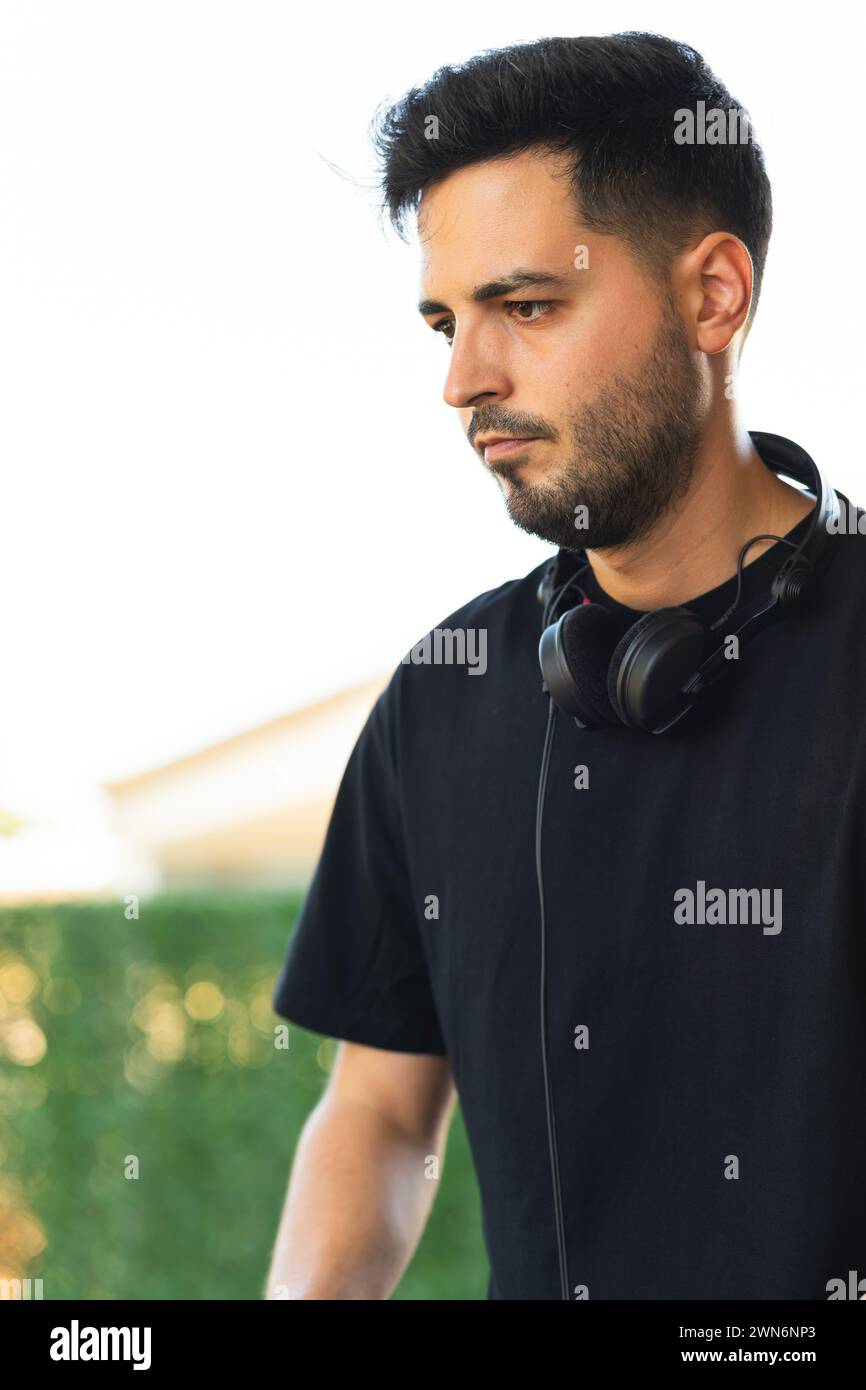 Portrait of a young dj dressed in black with headphones hanging on his ...