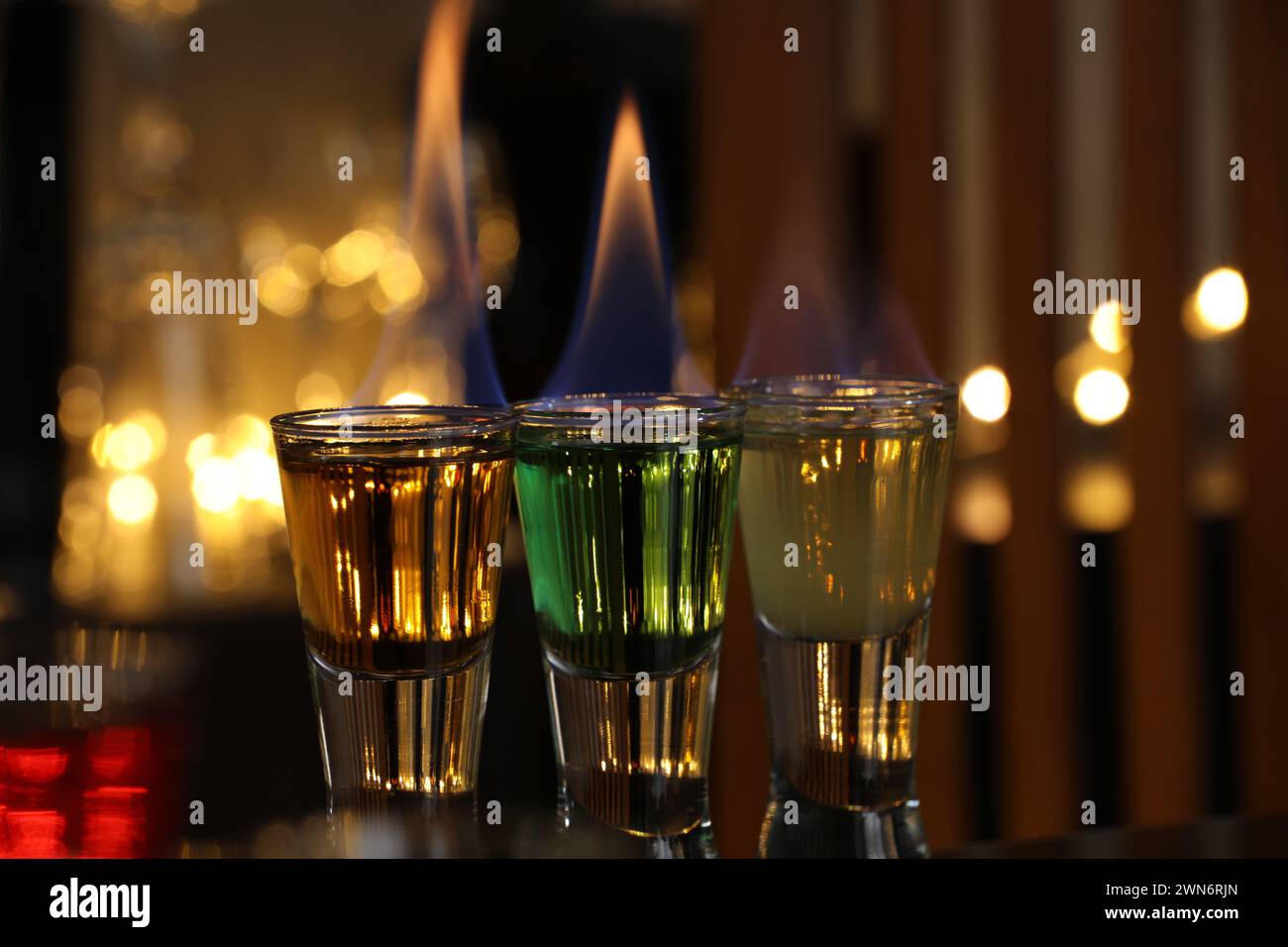 Flaming shooters in shot glasses on mirror surface against blurred ...