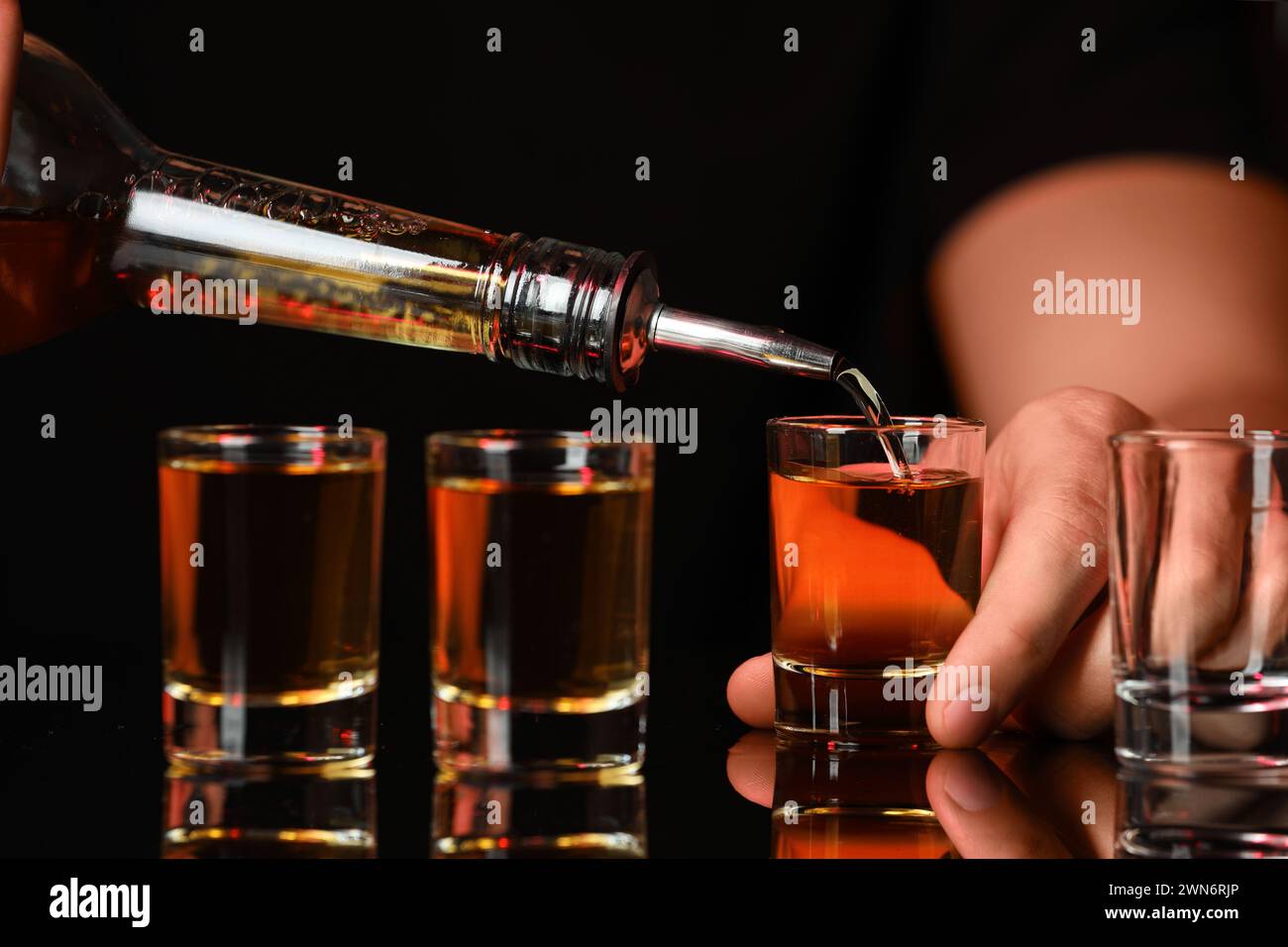 Bartender pouring alcohol drink into shot glass at mirror bar counter ...