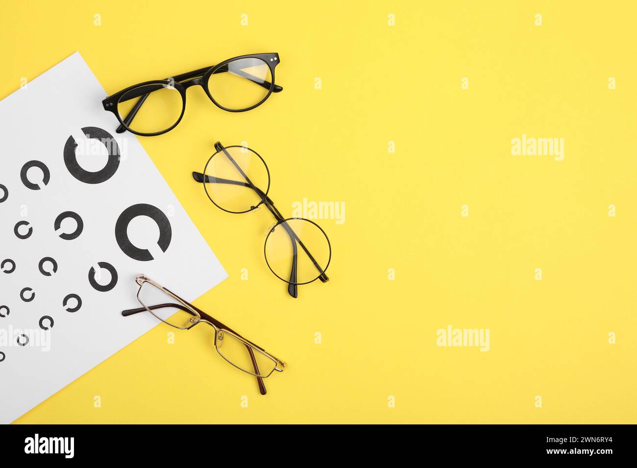 Vision test chart and glasses on yellow background, flat lay. Space for ...