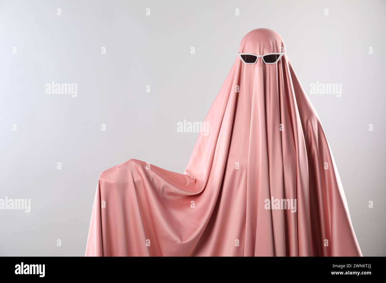 Glamorous ghost. Woman in pink sheet with sunglasses on light grey ...