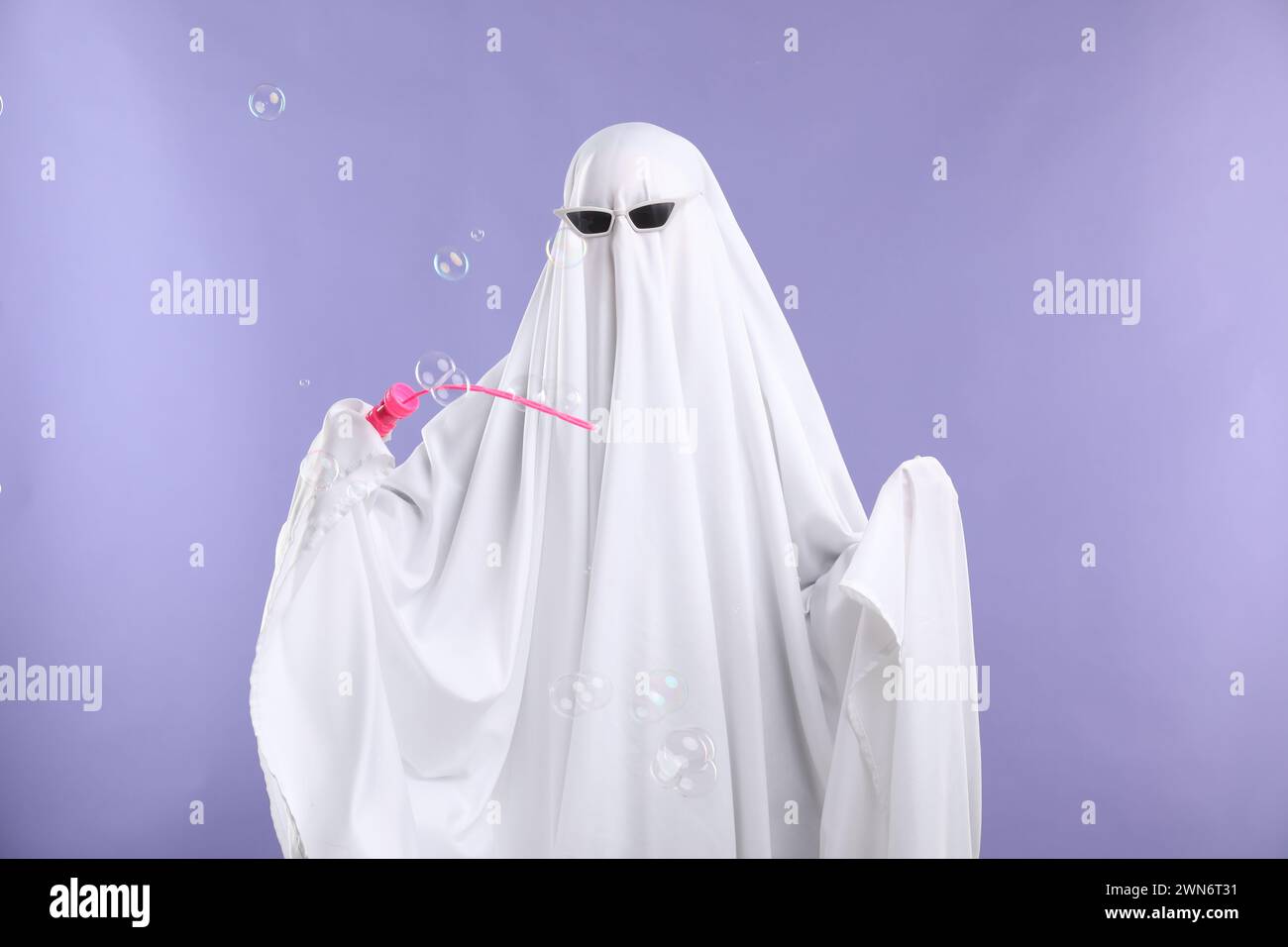 Funny ghost. Person in white sheet and sunglasses blowing soap bubbles ...