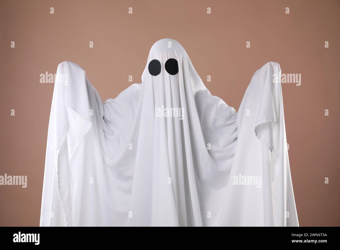 Creepy ghost. Person covered with white sheet on dark beige background ...