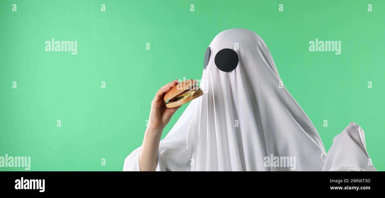 Creepy ghost. Person in white sheet with tasty hamburger on green ...