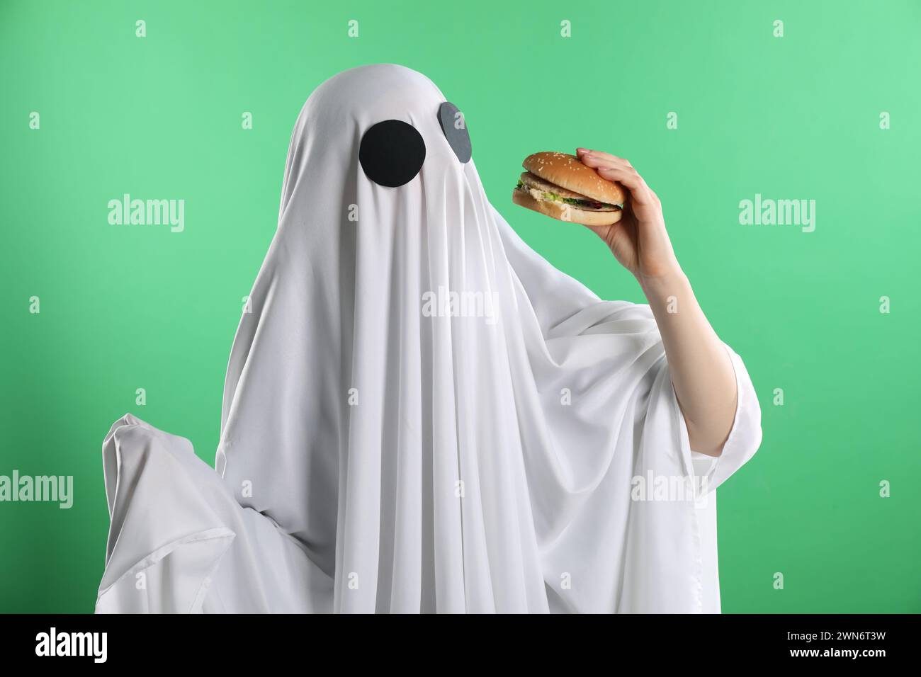 Creepy ghost. Person in white sheet with tasty hamburger on green ...