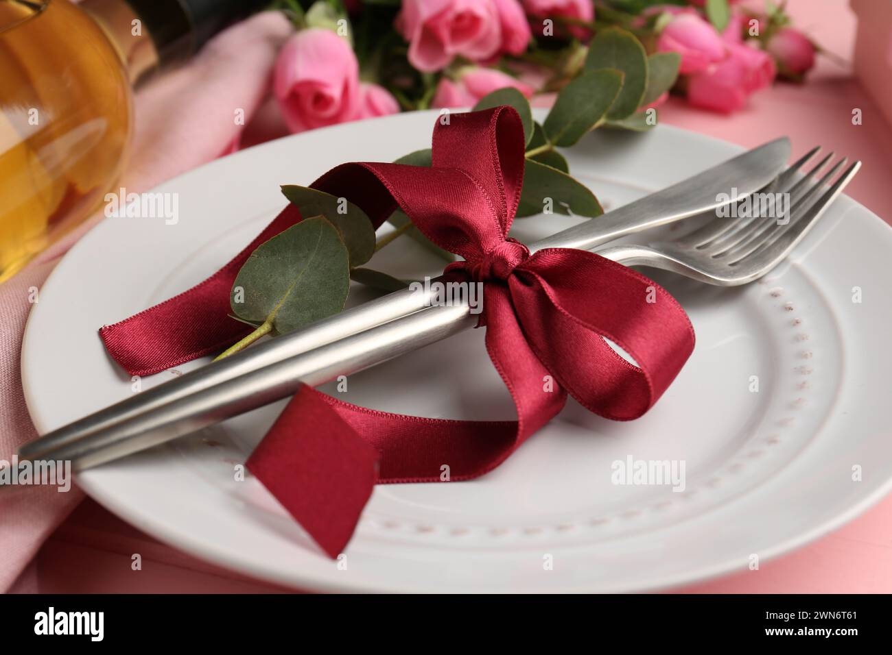 Romantic place setting. Plate, cutlery, eucalyptus branch and roses on ...
