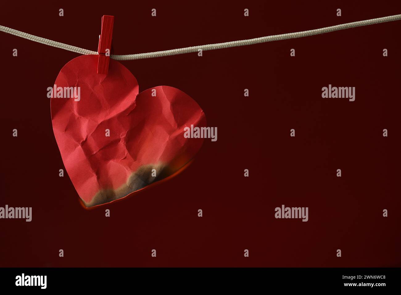 Crumpled red paper heart burning on rope against burgundy background ...