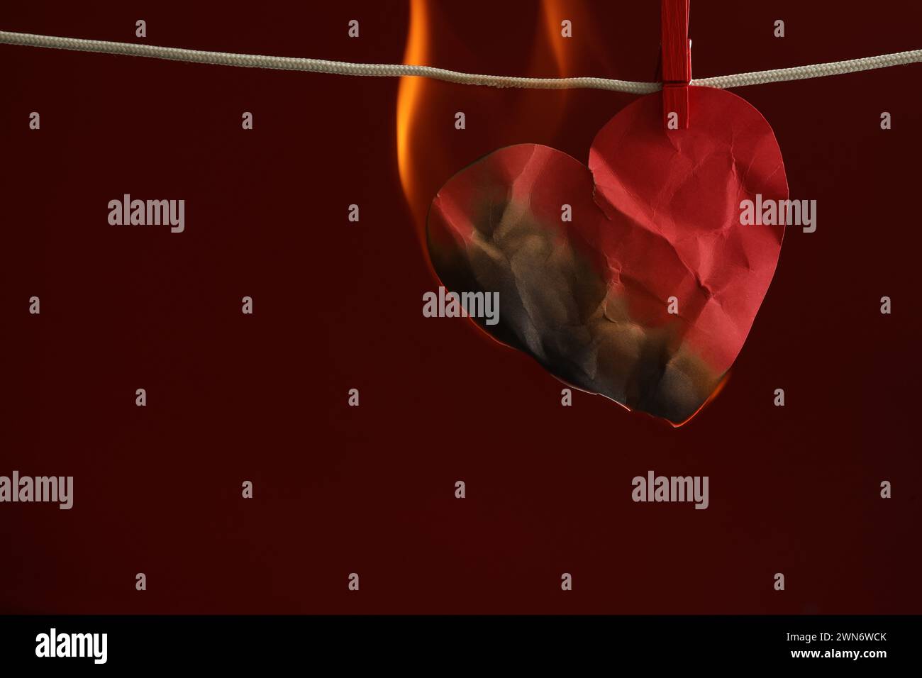 Crumpled red paper heart burning on rope against burgundy background ...