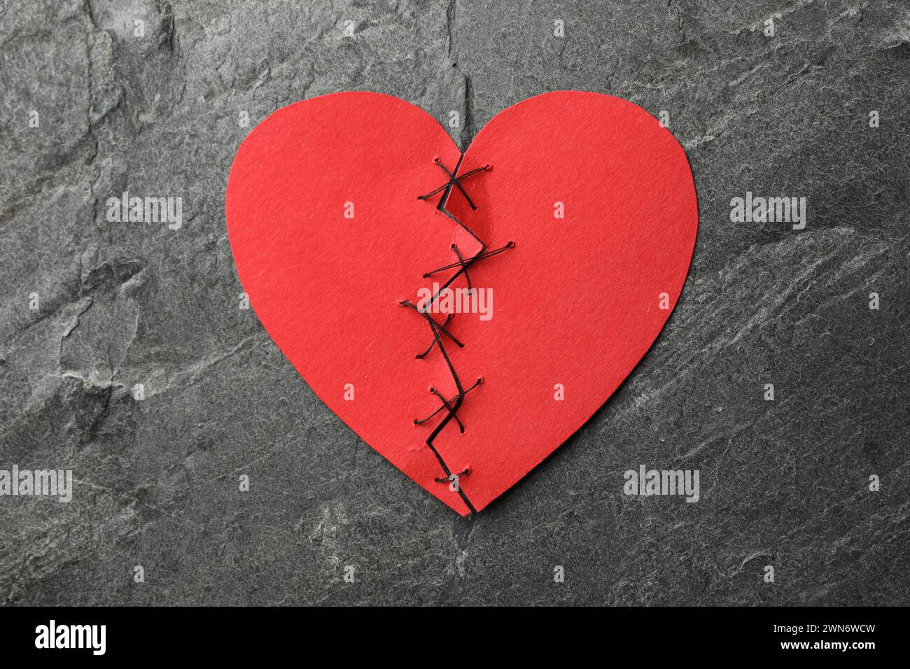 Broken heart. Torn red paper heart sewed with thread on dark grey table ...