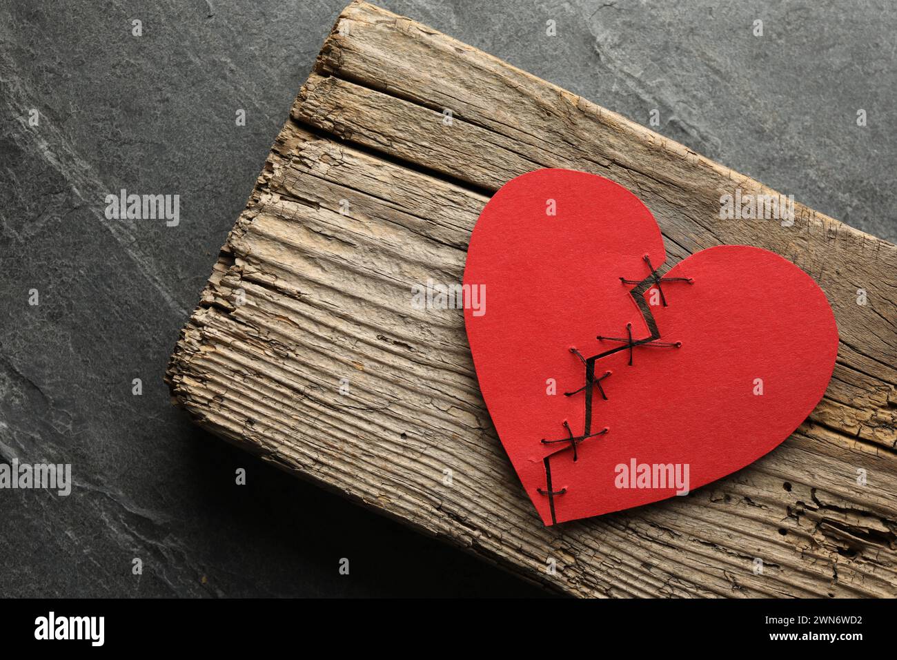 Broken heart. Torn red paper heart sewed with thread on grey table, top ...