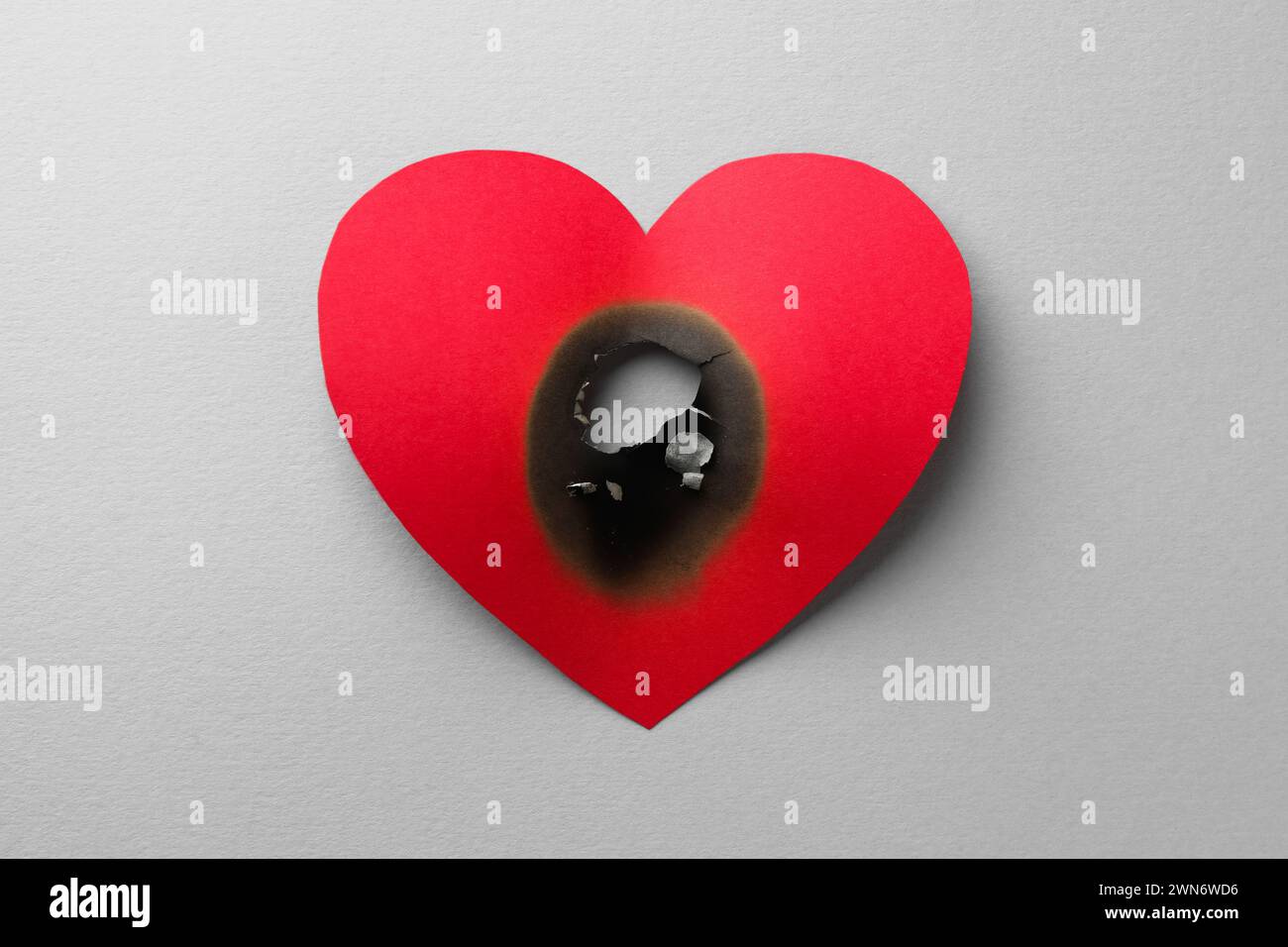 Red paper heart with burnt hole on white background, top view. Broken ...