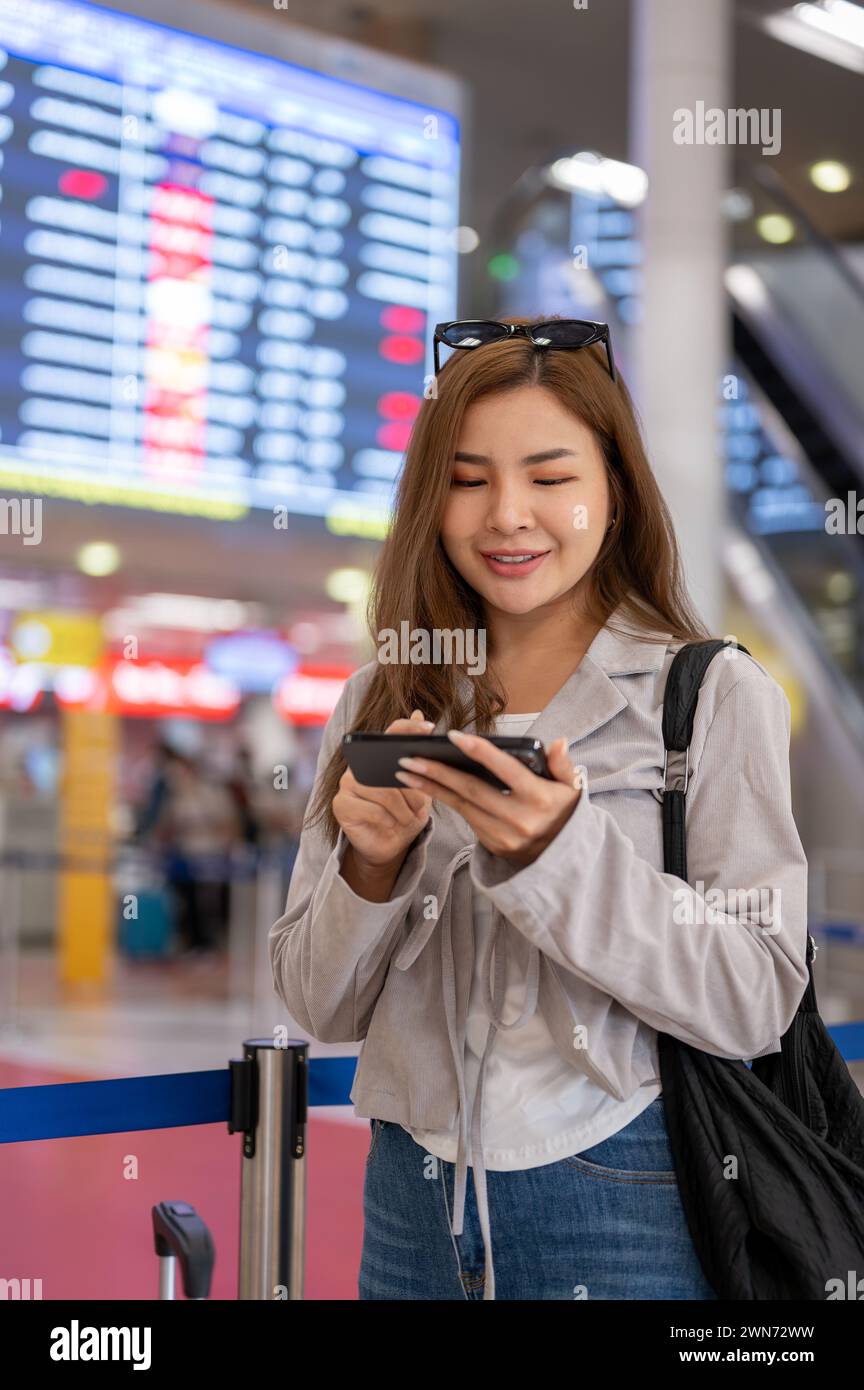 An attractive Asian female passenger is using her smartphone to check her flight boarding time ...