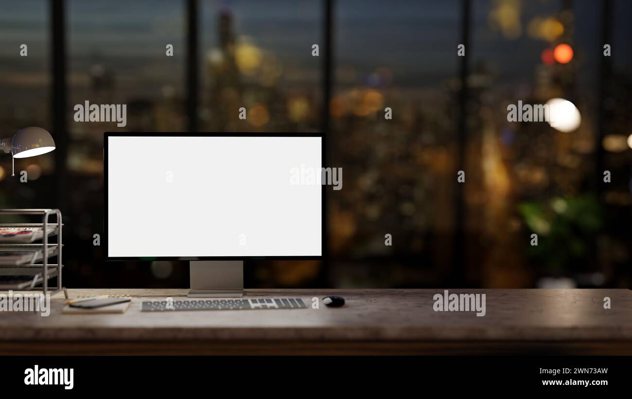 A computer desk in a modern dark office at night with a city view ...
