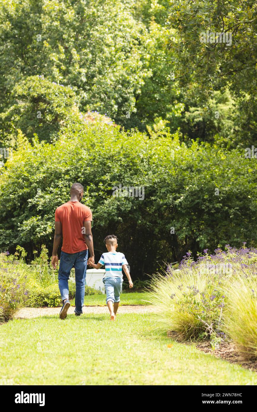 African American father and son walk together in a lush garden with ...