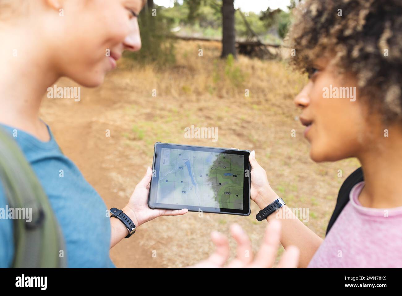 Two women are examining a map on a tablet during a hike in the woods on ...