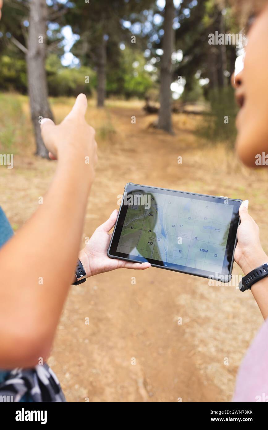 Young woman holds a tablet displaying a map, friend gestures towards ...