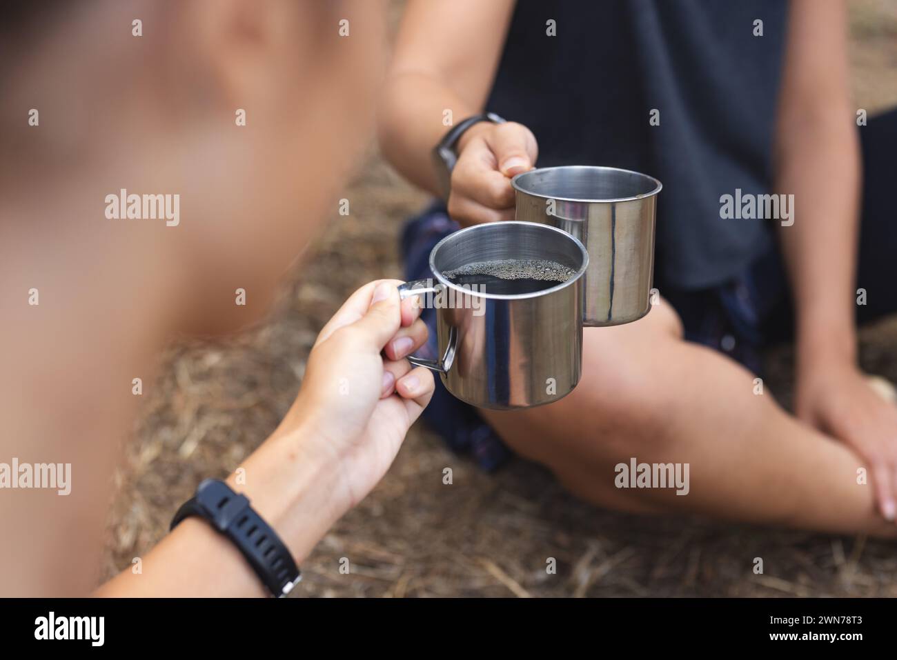 Two people are holding stainless steel cups, sharing a drink outdoors ...