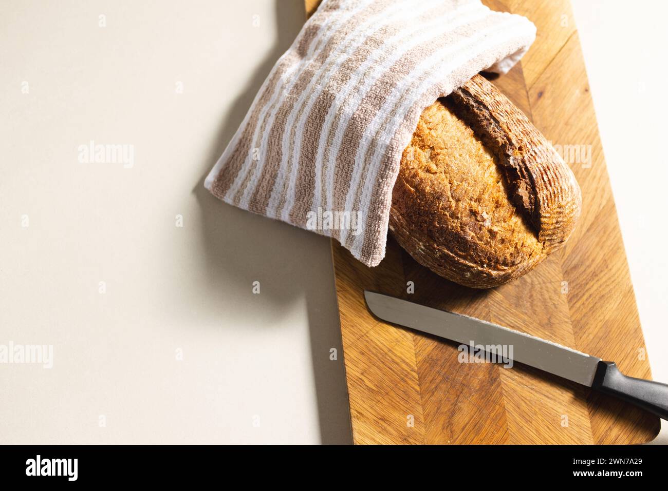A freshly baked loaf of bread rests on a wooden cutting board beside a ...