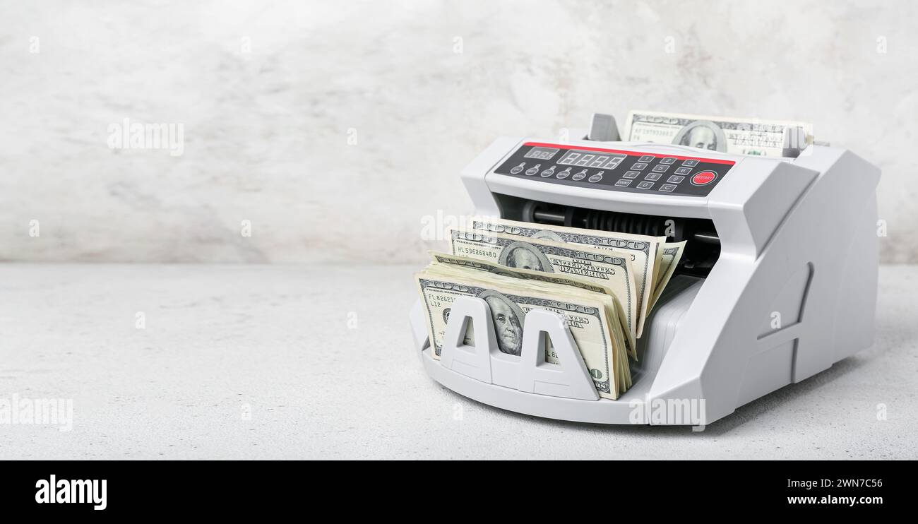 Modern cash counting machine with dollar banknotes on light background ...