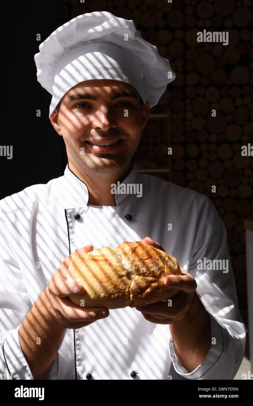 Young chef with loaf of fresh bread in bakery near window Stock Photo ...