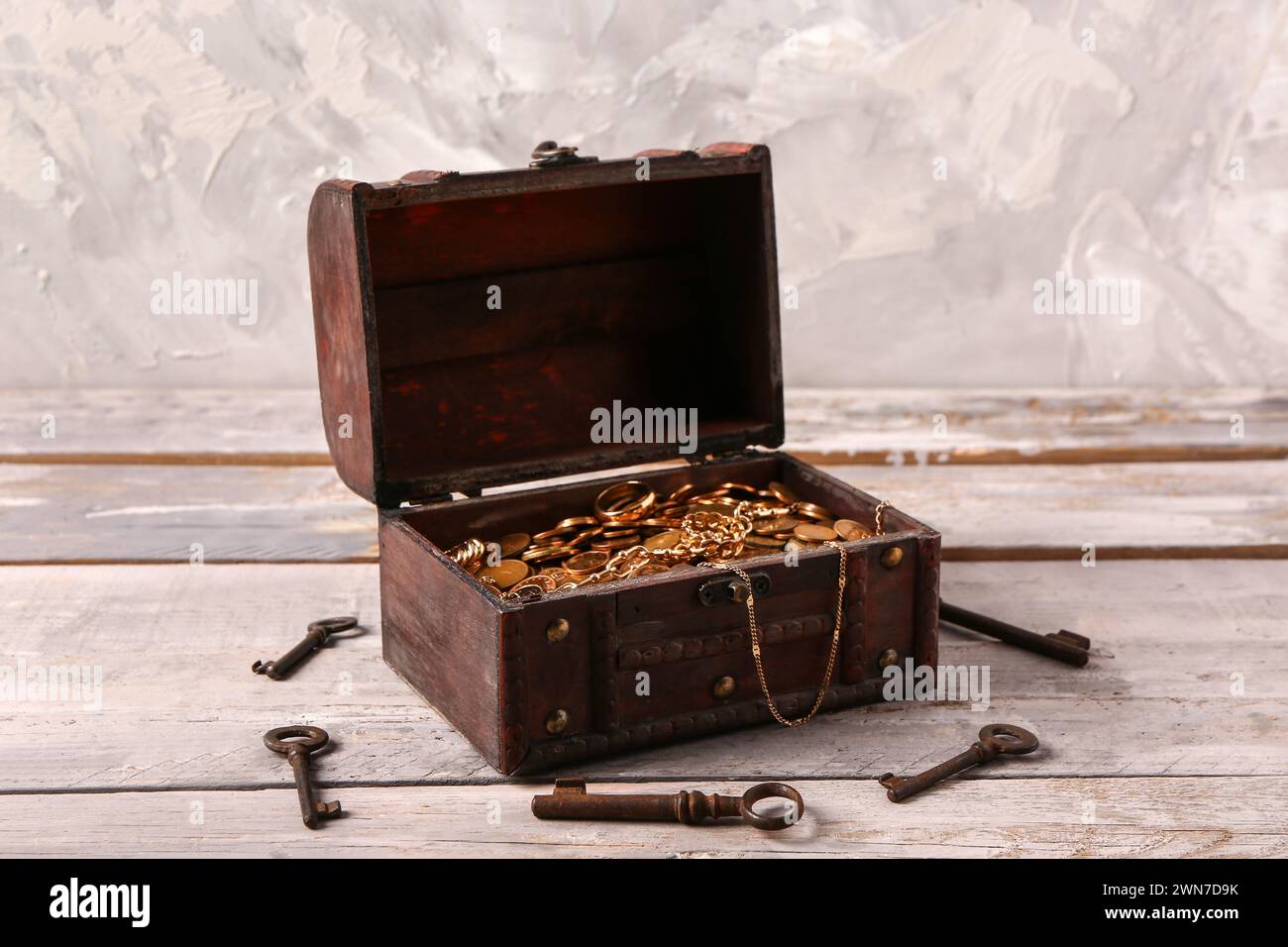 Old chest with treasures and keys on light wooden table near grunge ...