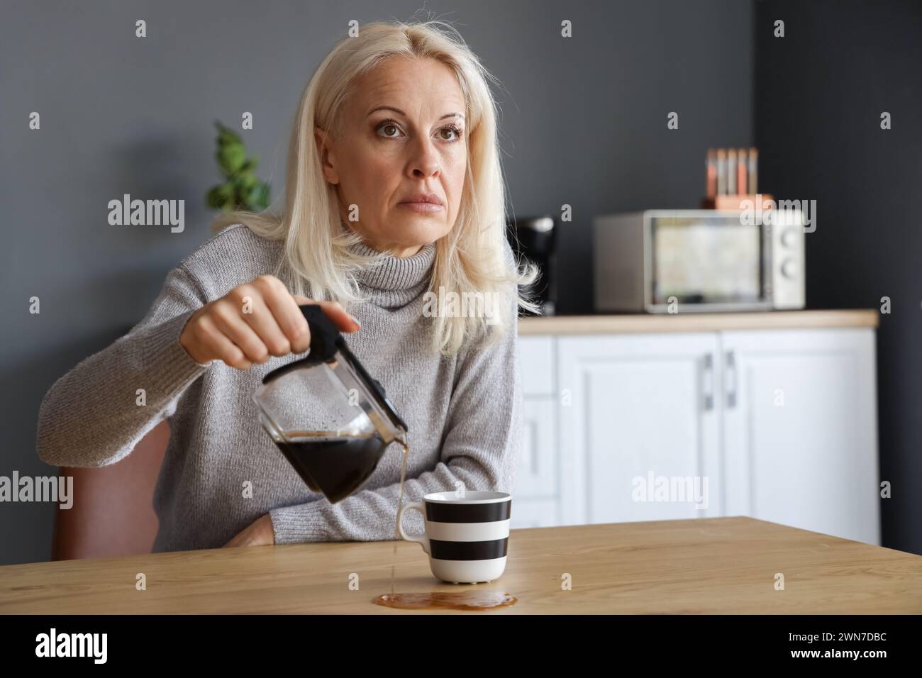 Depressed mature woman pouring coffee in kitchen Stock Photo - Alamy