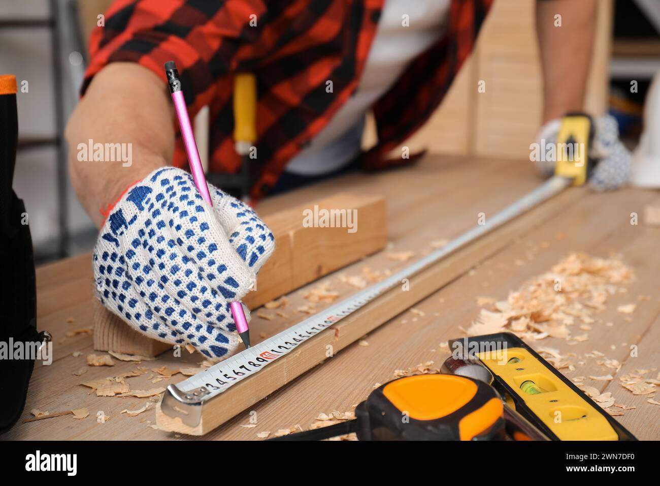 Male carpenter measuring plank length with tape at table in workshop ...