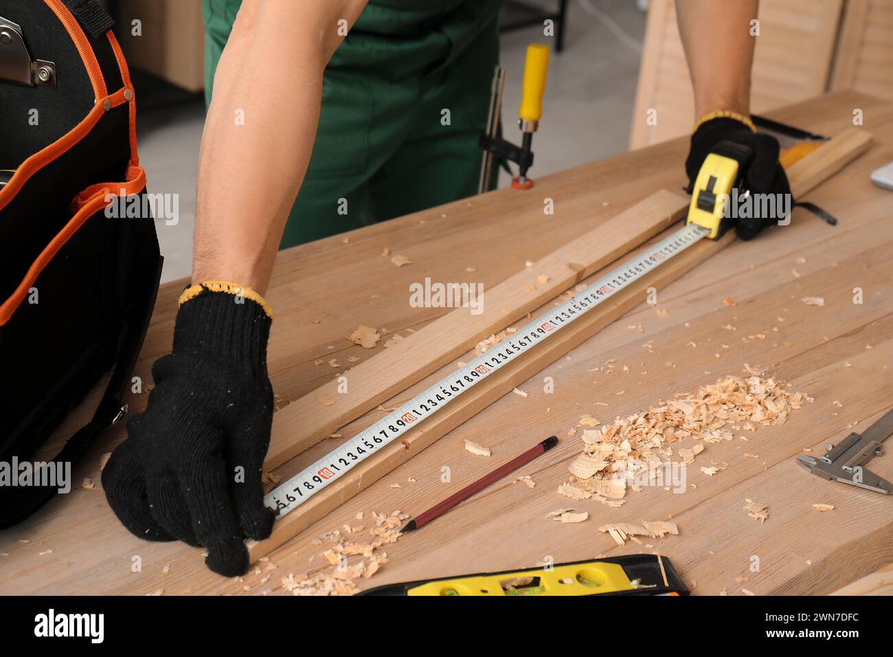Male carpenter measuring plank length with tape at table in workshop ...
