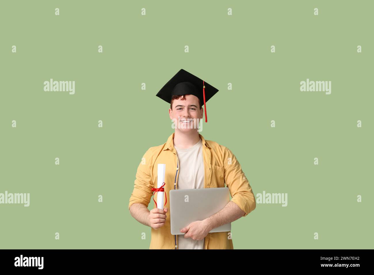 Male student in mortar board with diploma and modern laptop on green ...