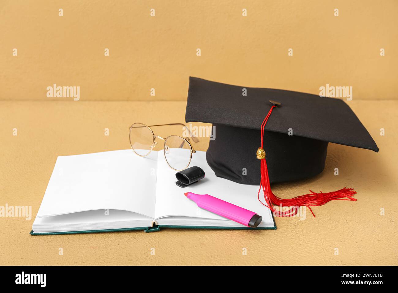 Mortar board with notebook, marker and eyeglasses on brown background ...