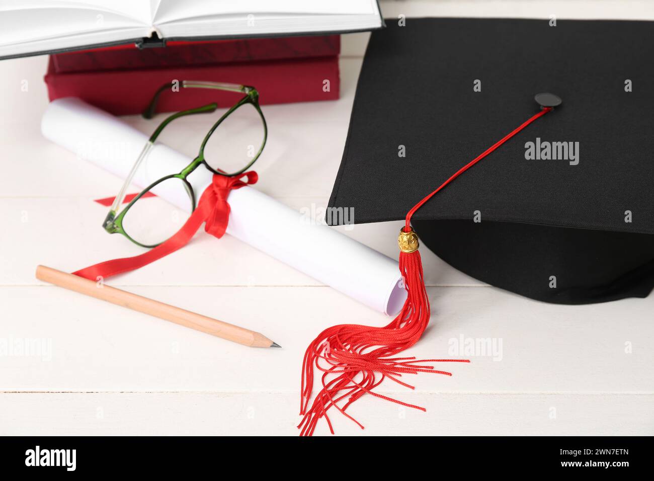 Mortar board with diploma, eyeglasses and notebooks on white wooden ...