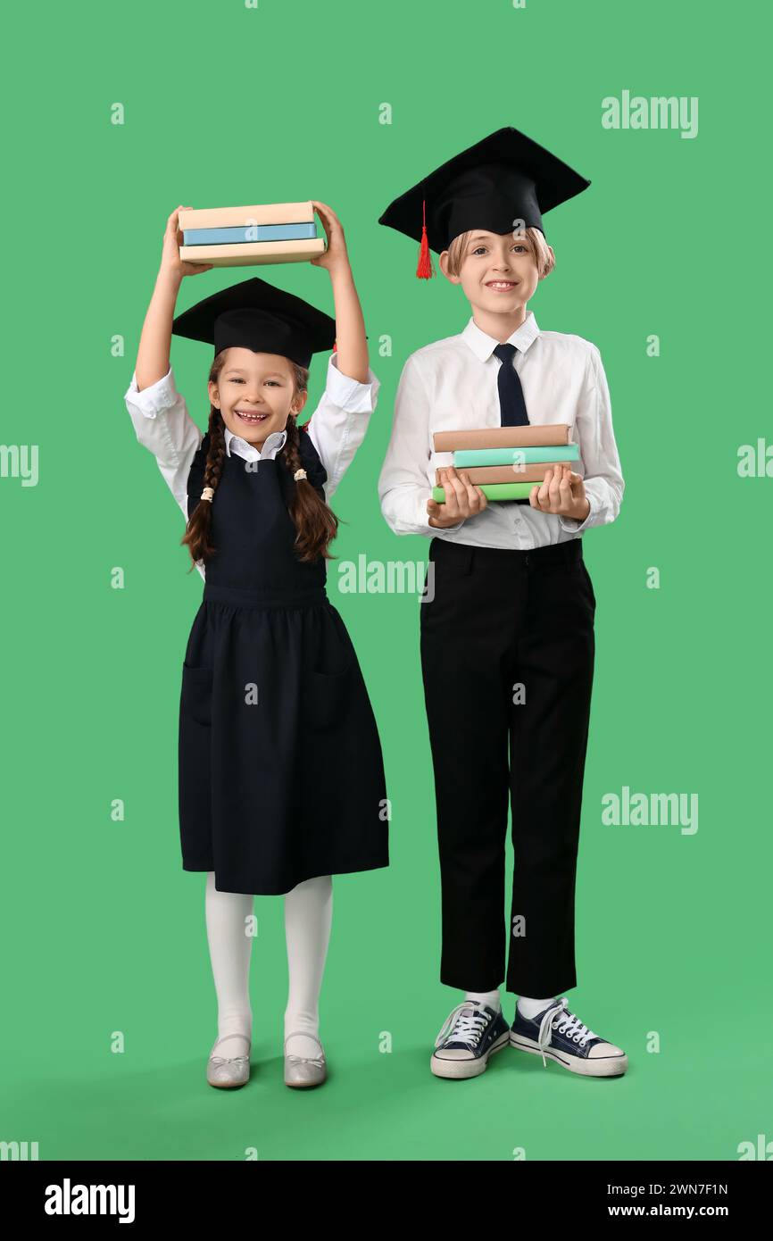 Little children in graduation hats with books on green background. End ...