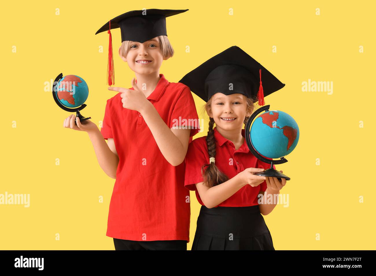 Little children in graduation hats with globes on yellow background ...