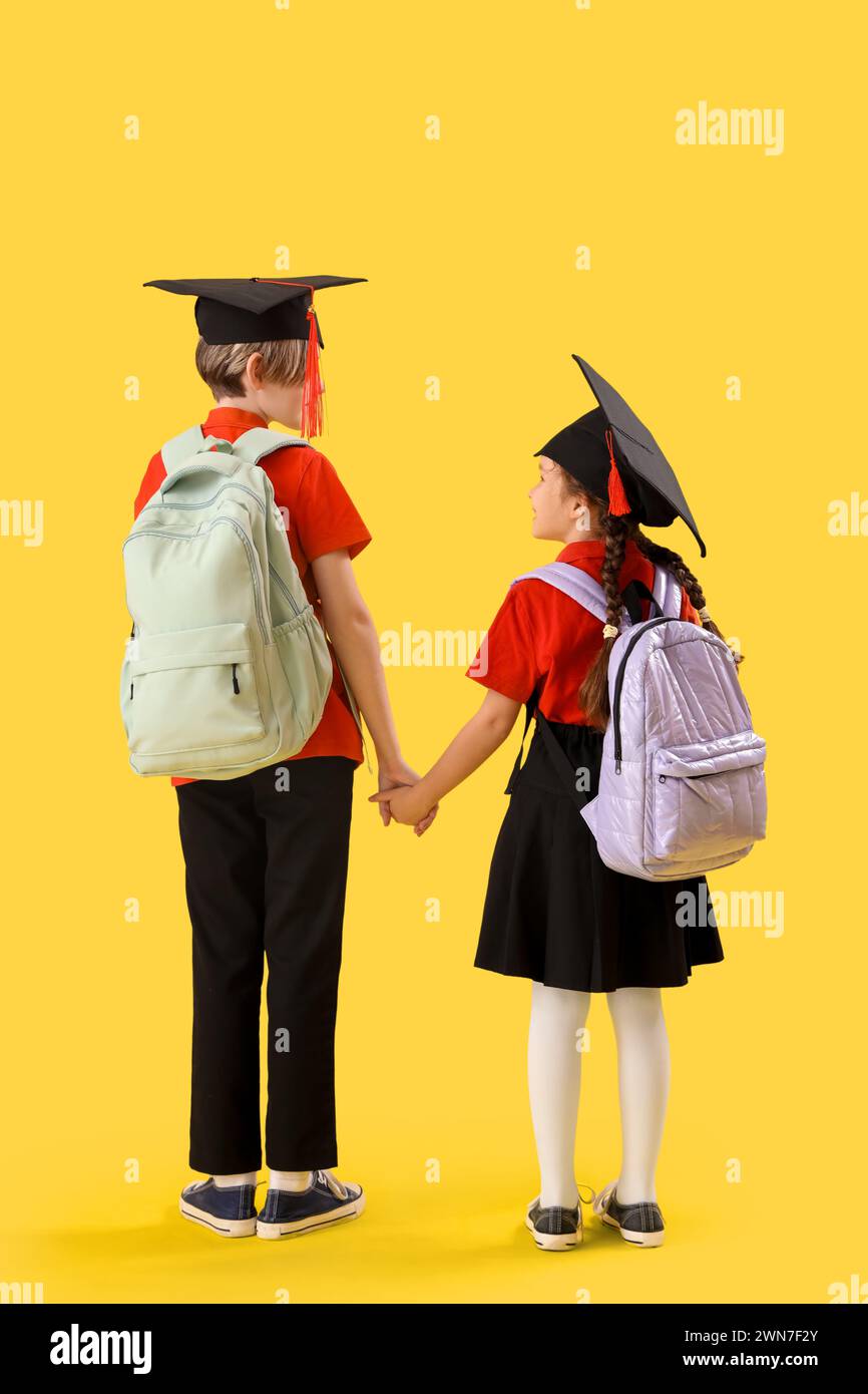 Little children in graduation hats on yellow background, back view. End ...