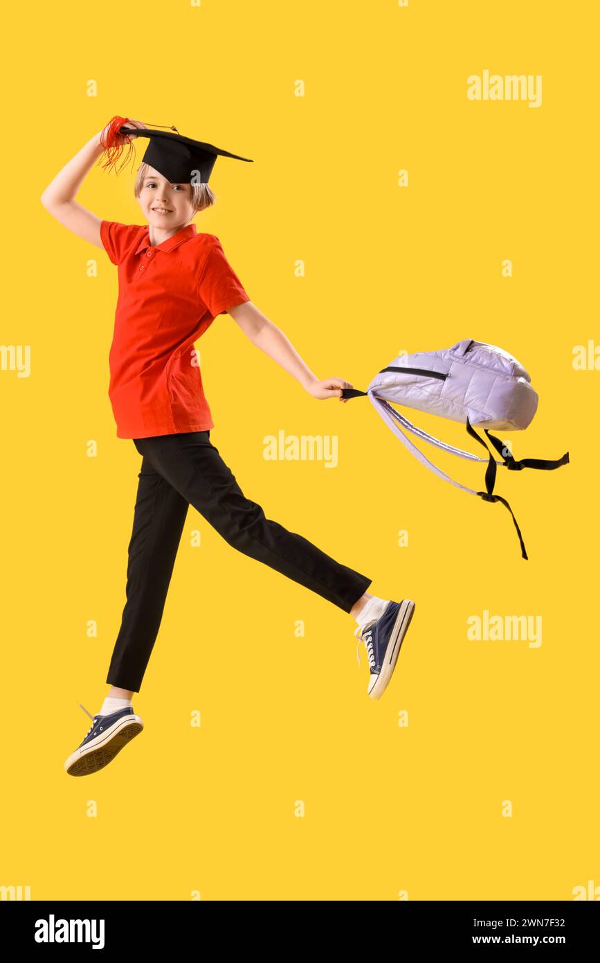 Little boy in graduation hat with backpack jumping on yellow background ...
