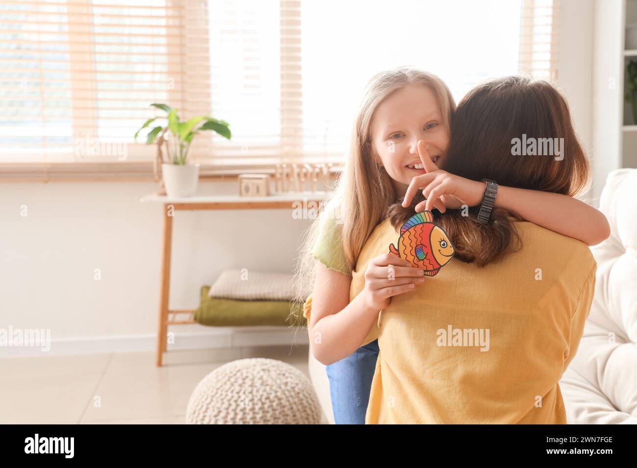 Funny little girl with paper fish hugging her mother at home. April ...