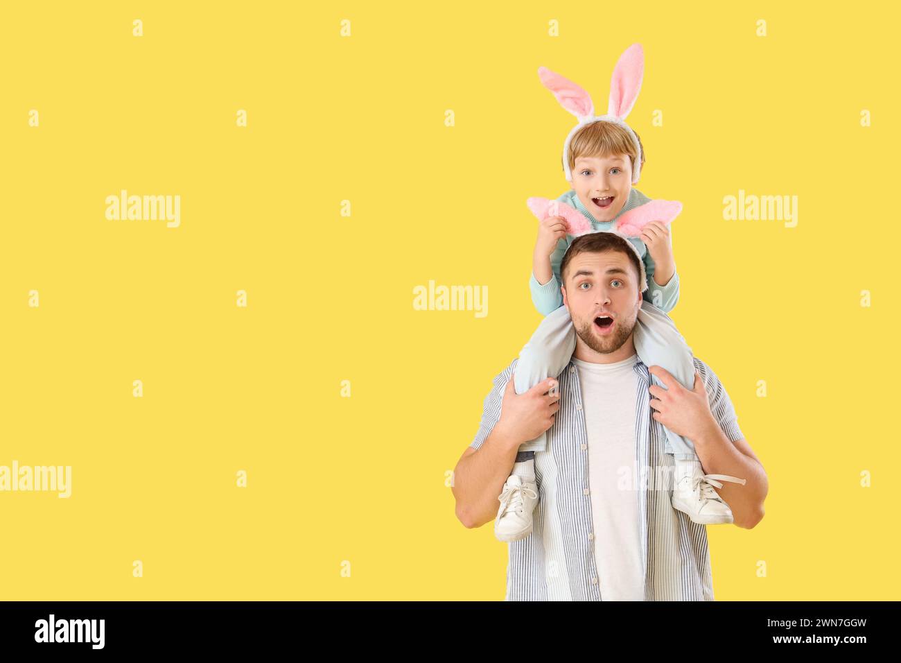 Surprised father with his little son in bunny ears on yellow background ...