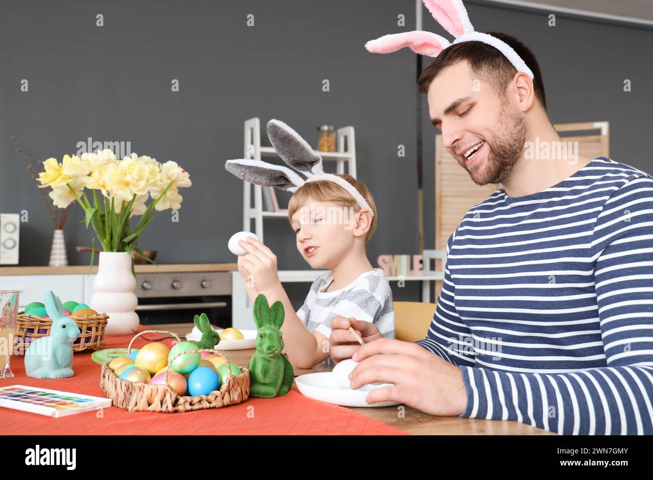 Cute little boy with his father painting Easter eggs at table in ...