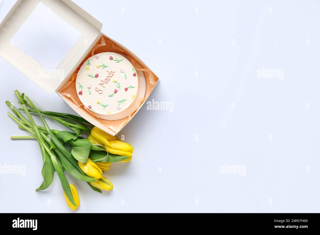 Box with sweet bento cake and beautiful yellow tulips on white ...