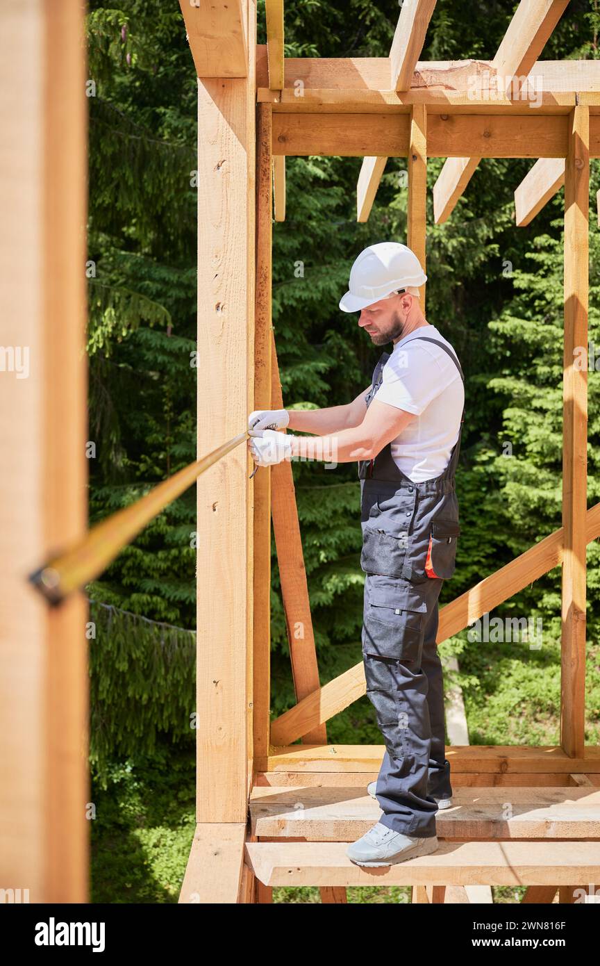 Carpenter constructing wooden skeleton building. Man measures distances ...