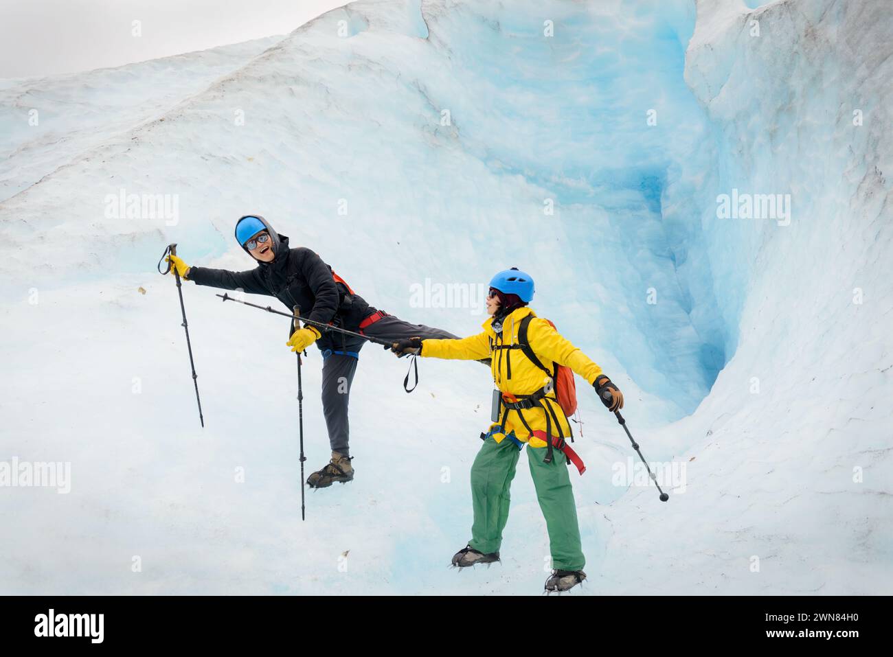 Couple holding hiking poles and doing yoga poses in front of an ice ...
