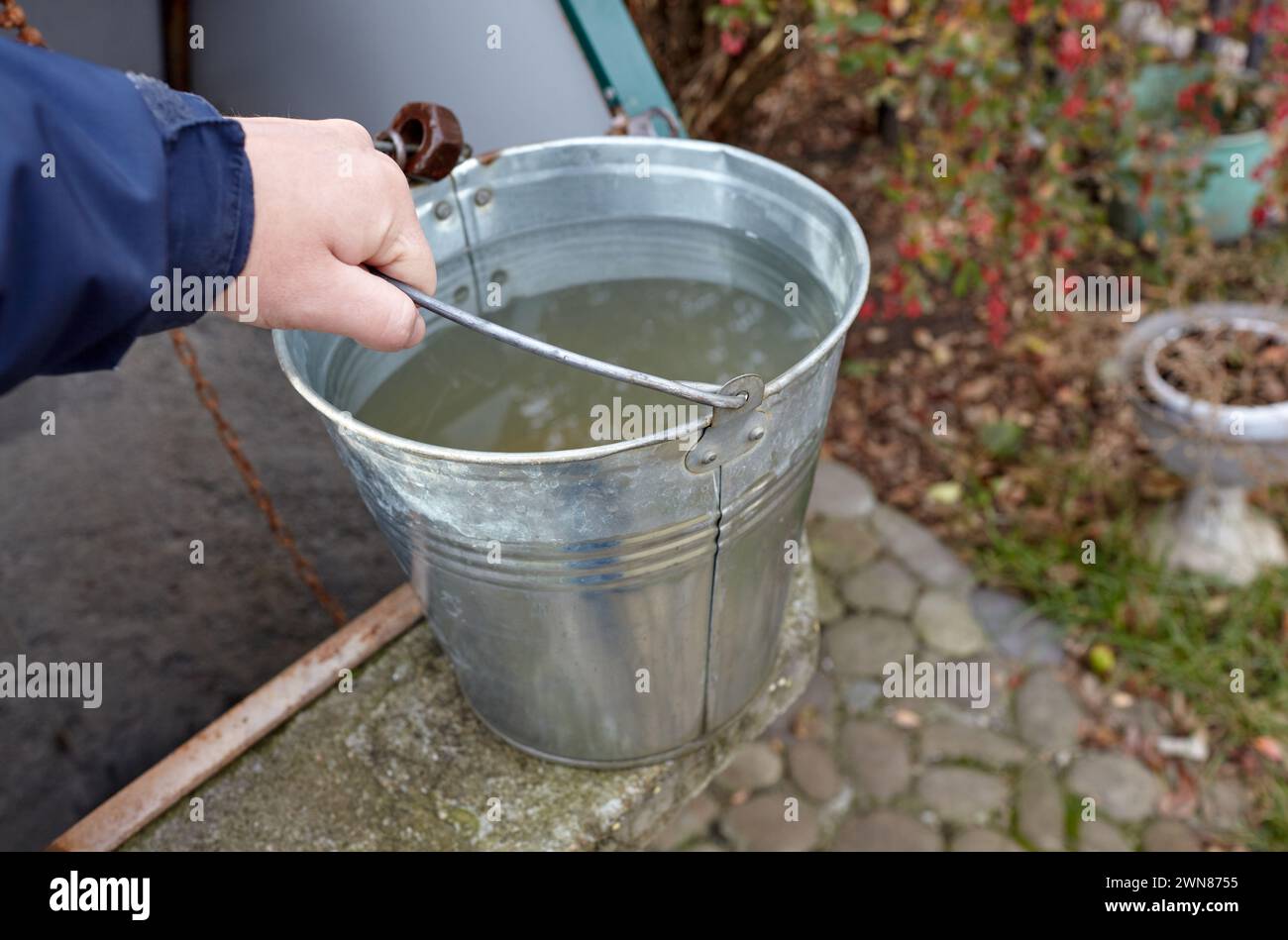 Man hand holding metal bucket with fresh water. Water from a deep well ...