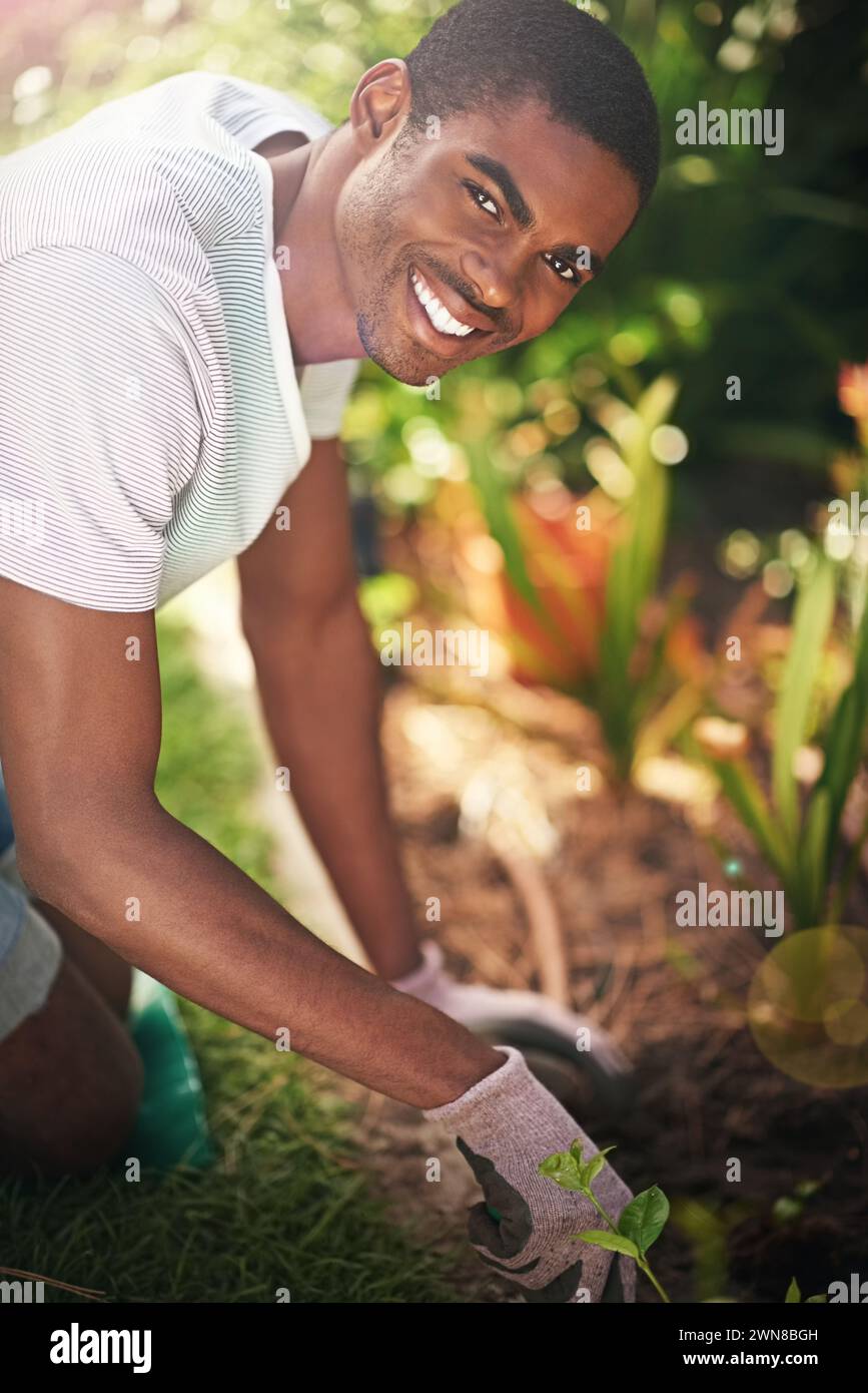 Portrait, nature and planting flowers with black man in garden of home ...