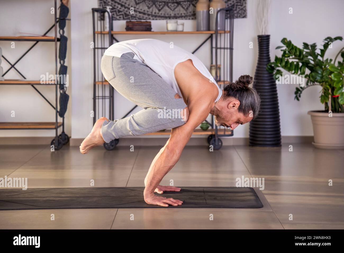 Side view of fit guy with ponytail practicing Kakasana pose on mat ...