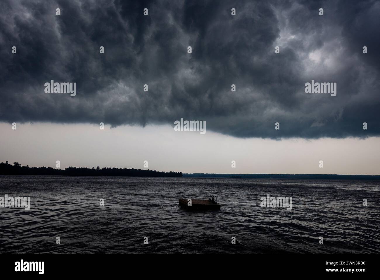 A lone dock floating on a lake with ominous storm clouds overhead Stock ...