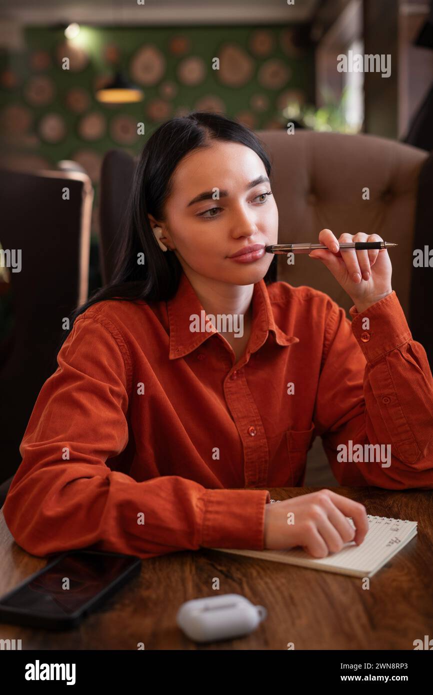 Pensive young female writer with notepad and pen looking away and ...